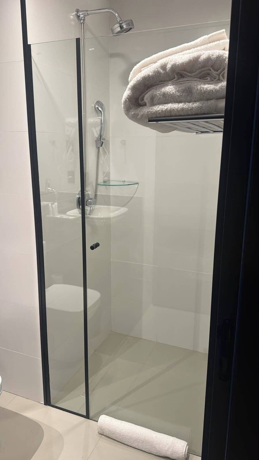 Um chuveiro com paredes de vidro, um prateleira de vidro, um vaso sanitário branco e uma toalha na prateleira.