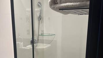 Um chuveiro com paredes de vidro, um prateleira de vidro, um vaso sanitário branco e uma toalha na prateleira.