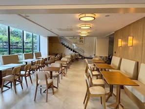 Uma sala de jantar moderna com mesas e cadeiras de madeira, uma escada e grandes janelas com vista para o verde.