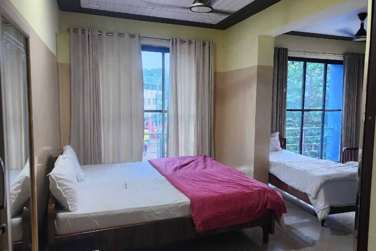 Quarto com duas camas, um ventilador de teto e janelas amplas com cortinas.