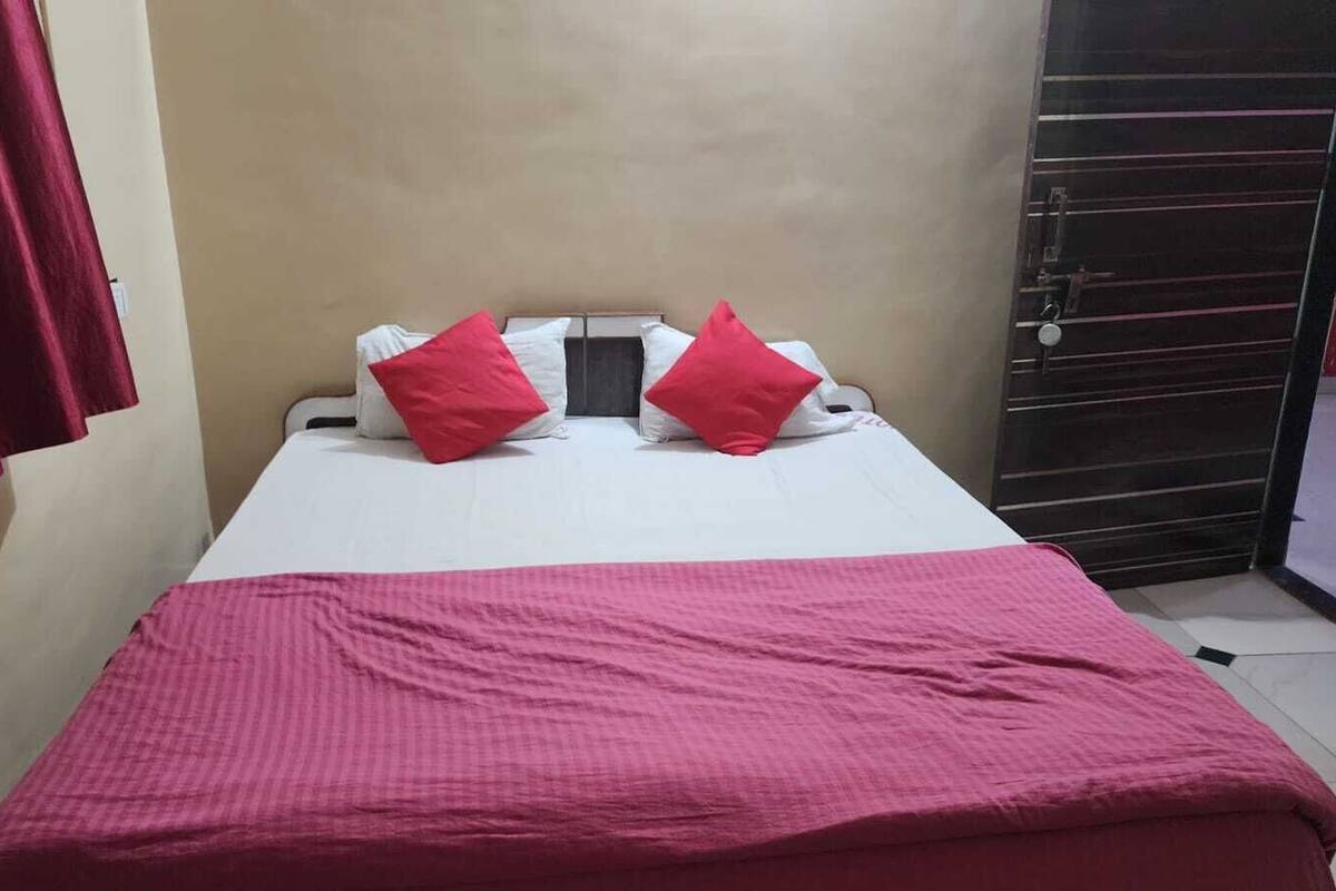 Uma cama de solteiro com um cobertor e almofadas vermelhos, uma porta fechada e uma cortina vermelha.