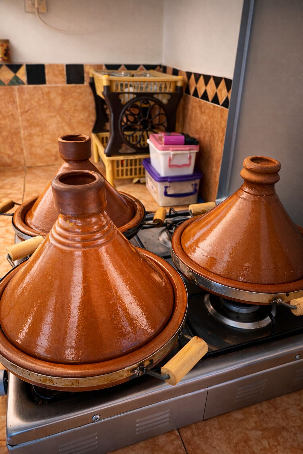 Uma cozinha com dois tajines no fogão, uma colher de pau e uma estante de temperos.
