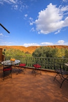 Um terraço com mesa e cadeiras, vista para colinas e céu claro.