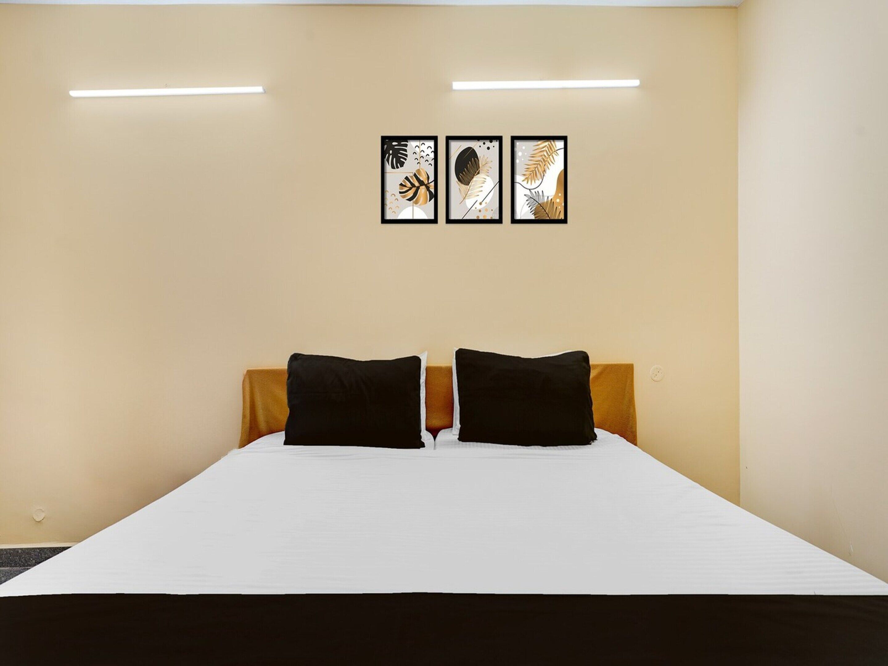 Quarto de hotel com cama, duas almofadas pretas, cabeceira de madeira e três quadros na parede.