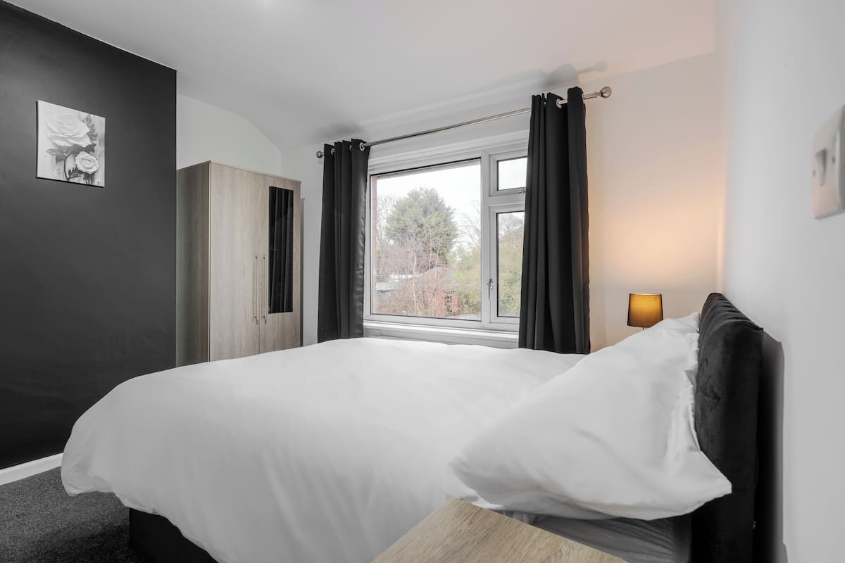 Quarto com cama, janela com cortinas, luminária de cabeceira e um quadro na parede.