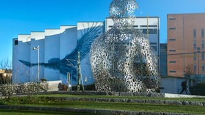 Escultura metálica esférica em frente a um edifício moderno, com céu claro.