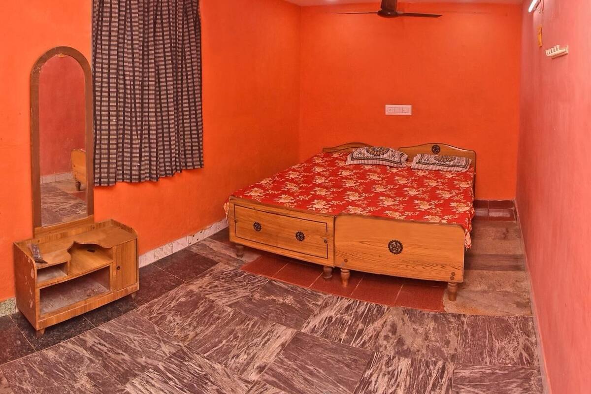 Quarto com cama, espelho, ventoinha no teto e um pequeno armário de madeira.