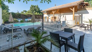 Uma área de piscina com espreguiçadeiras e guarda-sóis, um deck cercado e um edifício com fachada de madeira.