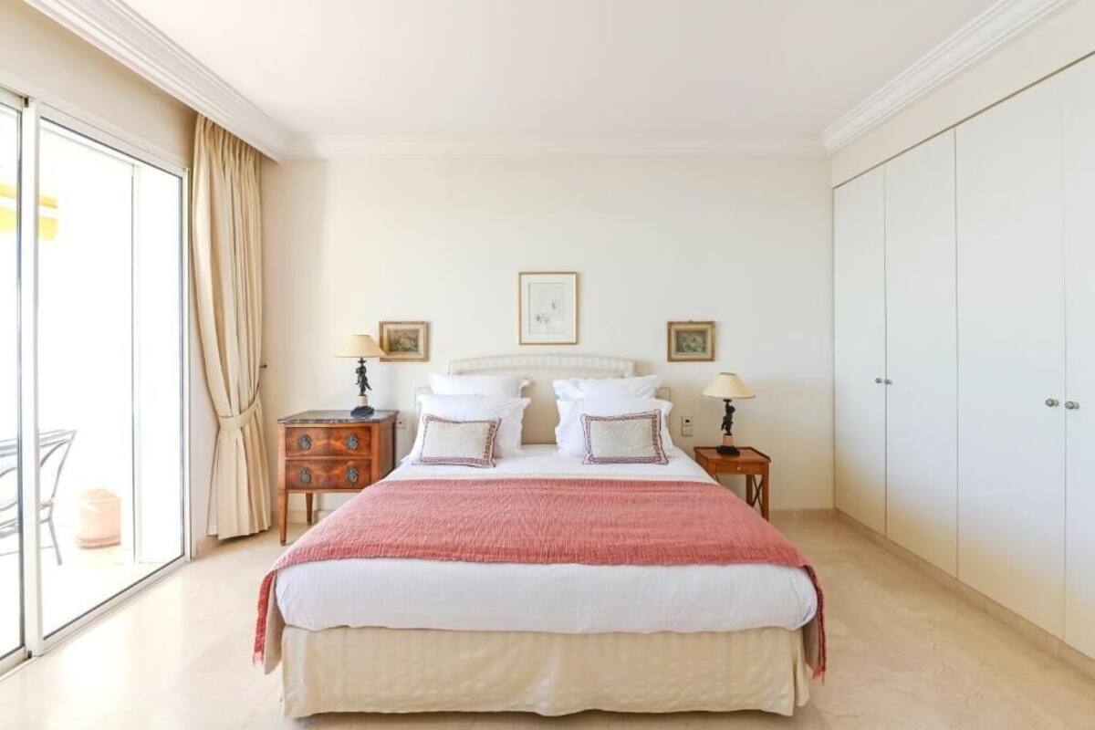 Quarto com uma cama, duas mesas de cabeceira, um guarda-roupa e uma janela grande com cortinas.