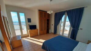 Quarto com cama, televisão, guarda-roupa e varanda com vista.