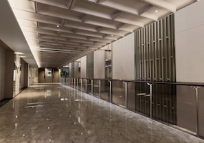 Um corredor moderno e espaçoso, com piso refletivo, guarda-corpo de vidro e parede com padrão.