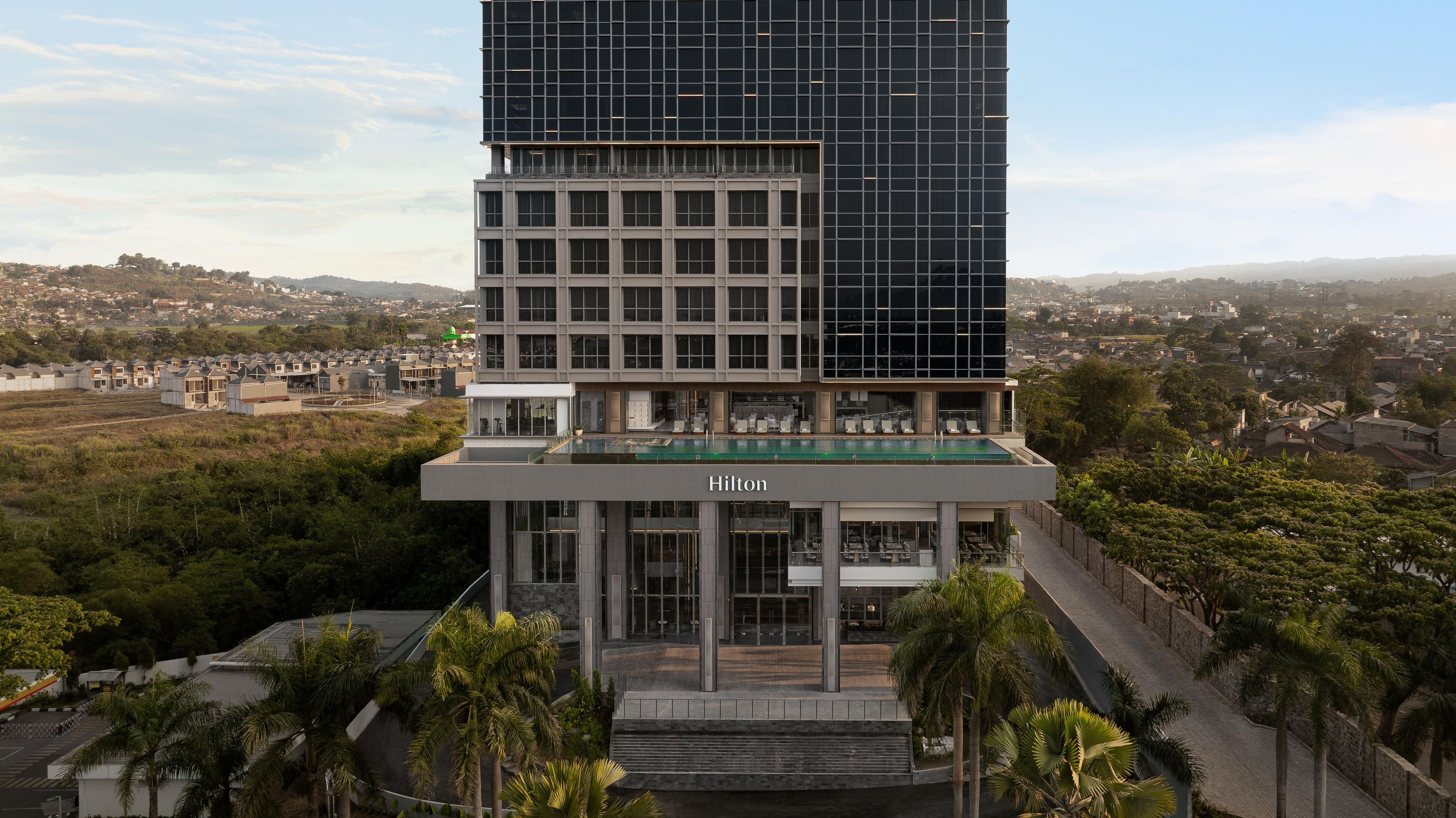 Um hotel moderno com piscina no terraço, rodeado por vegetação exuberante e vista para a paisagem urbana.