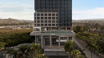 Um hotel moderno com piscina no terraço, rodeado por vegetação exuberante e vista para a paisagem urbana.