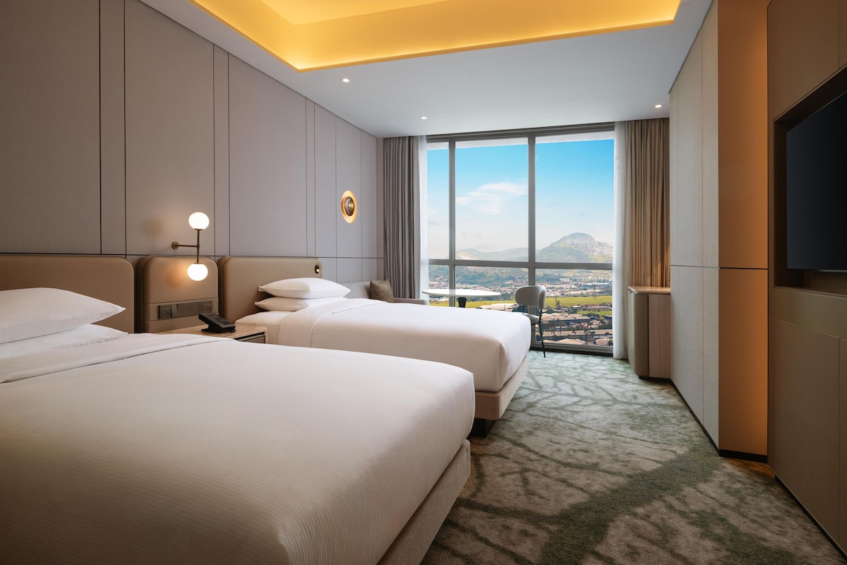 Quarto de hotel com duas camas, uma janela ampla com vista para a montanha e uma TV de tela plana.