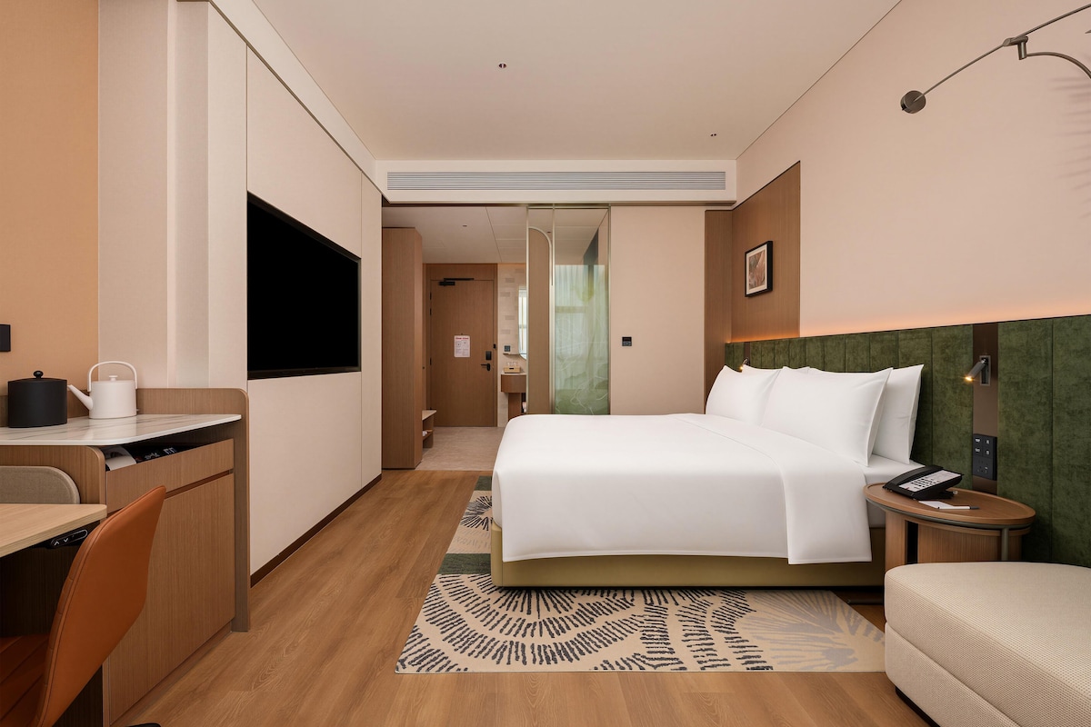 Quarto de hotel com cama, escrivaninha, cadeira e uma pequena mesa com chaleira.