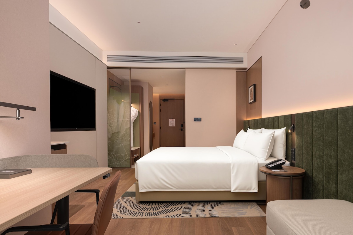 Quarto de hotel moderno com uma cama, mesa de cabeceira, escrivaninha e televisão de tela plana.