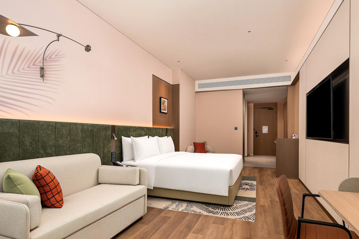 Quarto de hotel moderno com cama, sofá, escrivaninha e televisão.