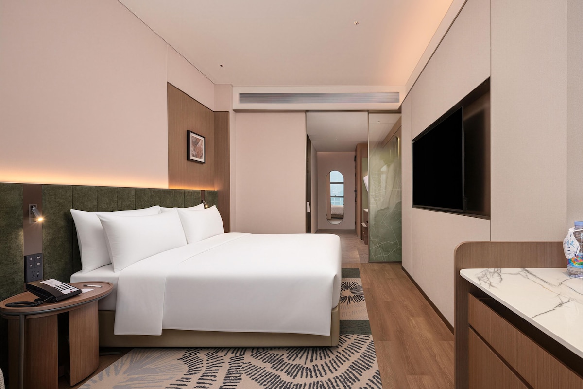 Quarto de hotel moderno com cama, mesa de cabeceira e televisão de tela plana.