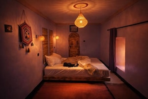 Um quarto com iluminação suave, uma cama, um candeeiro pendente e um abajur na parede.
