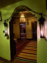 Um corredor com carpete listrado, um candelabro e luminárias fixadas na parede.