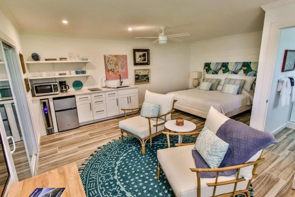 Quarto compacto com cama, mesa pequena para refeições, micro-ondas e geladeira.