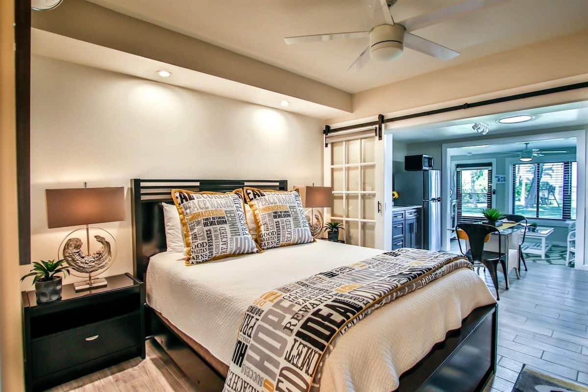 Quarto com cama, mesas de cabeceira, ventilador de teto e vista para o exterior.