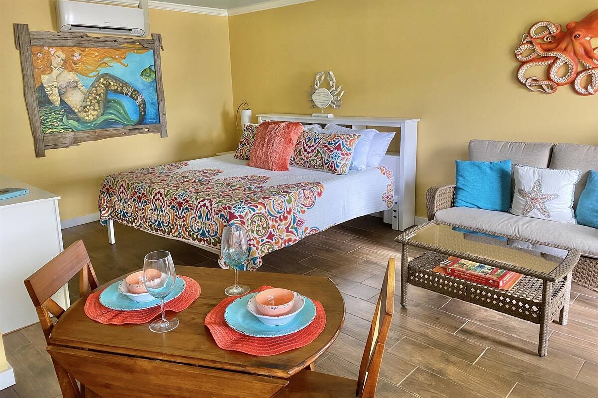 Quarto com cama, sofá, mesa de jantar com cadeiras e ar-condicionado fixado na parede.