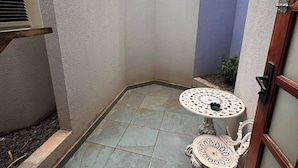 Um pequeno espaço de pátio ao ar livre com piso de azulejos, uma mesa redonda com tampo decorativo e uma cadeira com pés ornamentados.