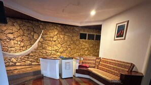 Quarto com parede de pedra, rede, sofá e um pequeno frigorífico.