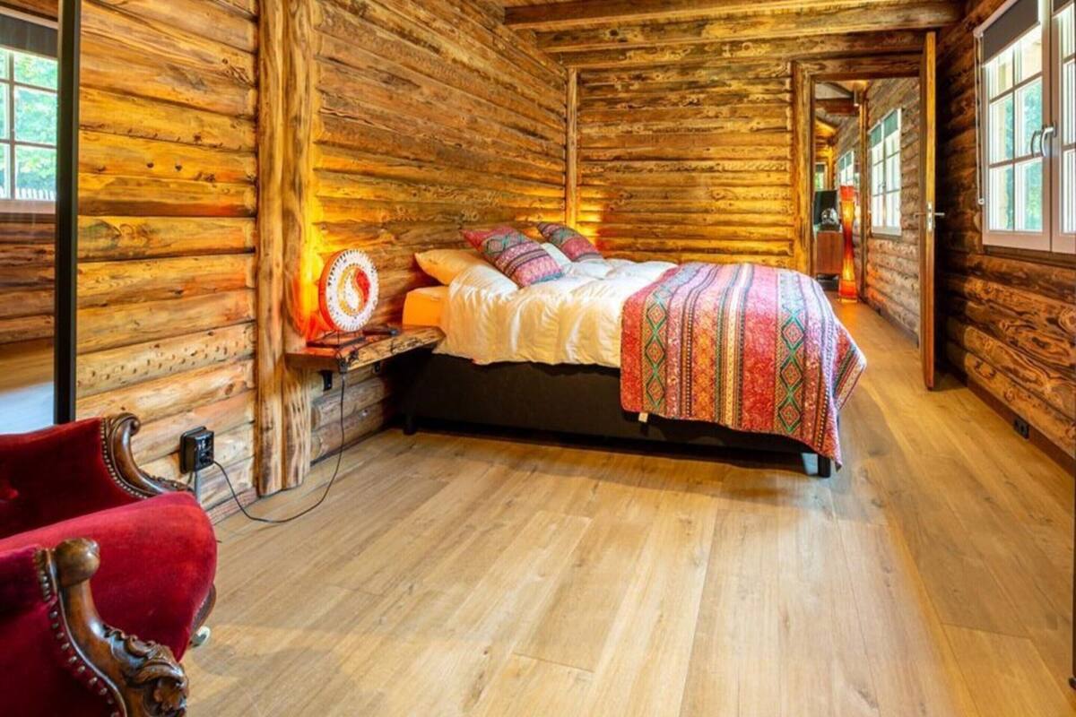 Quarto de cabana de tronco com uma cama, uma cadeira vermelha e piso de madeira.