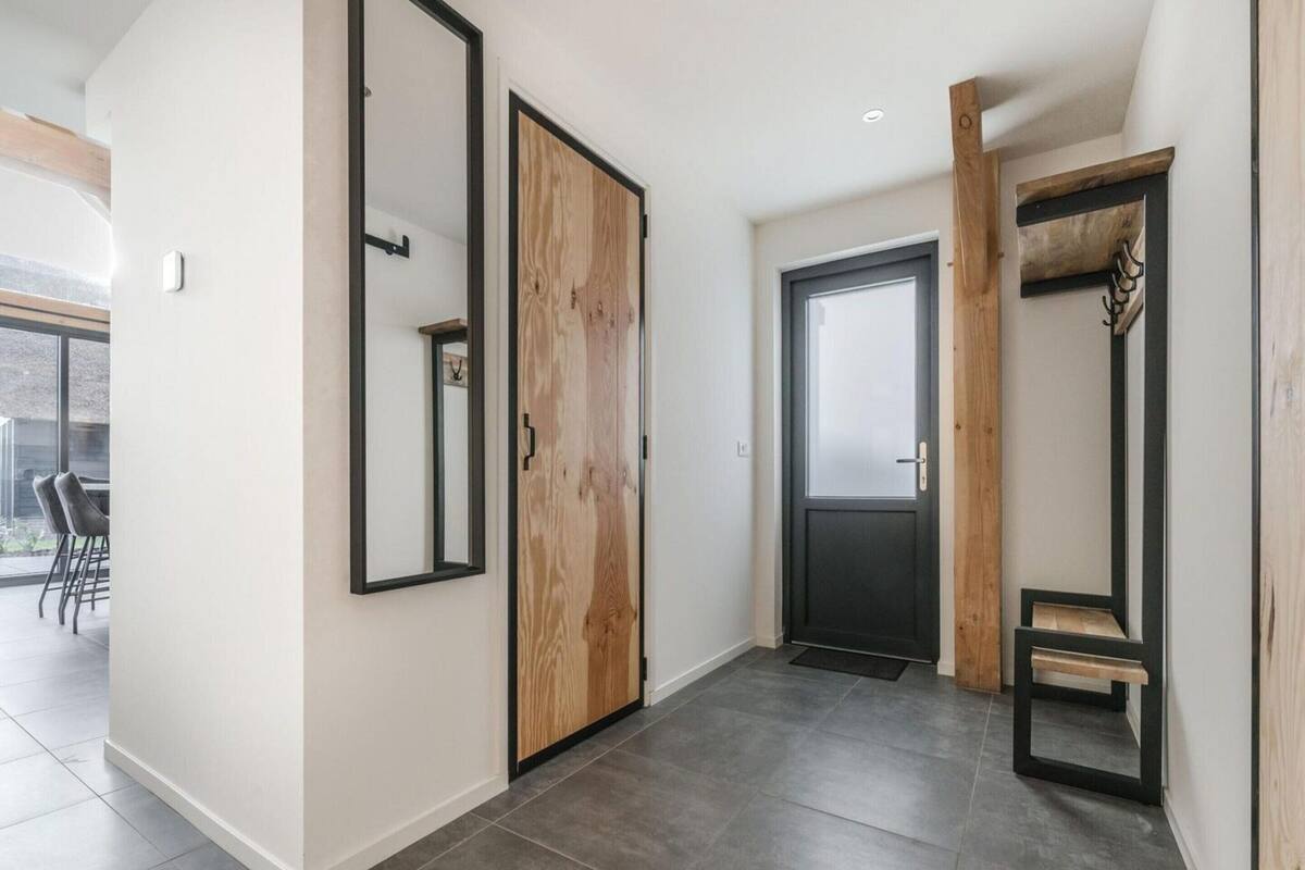 Um interior moderno com uma porta de madeira, um espelho com moldura preta e uma porta escura.