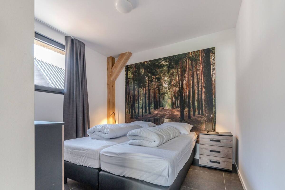 Quarto moderno com uma cama grande, uma mesa de cabeceira e um mural temático de floresta.
