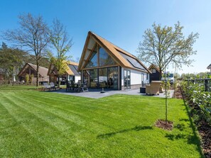 Uma casa moderna com um amplo terraço envidraçado, telhado inclinado e gramado bem cuidado.