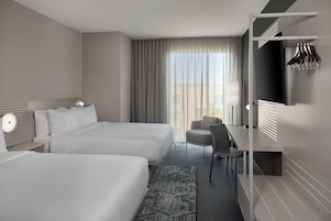 Quarto de hotel com duas camas, uma escrivaninha, uma cadeira, uma televisão e um porta-roupas.