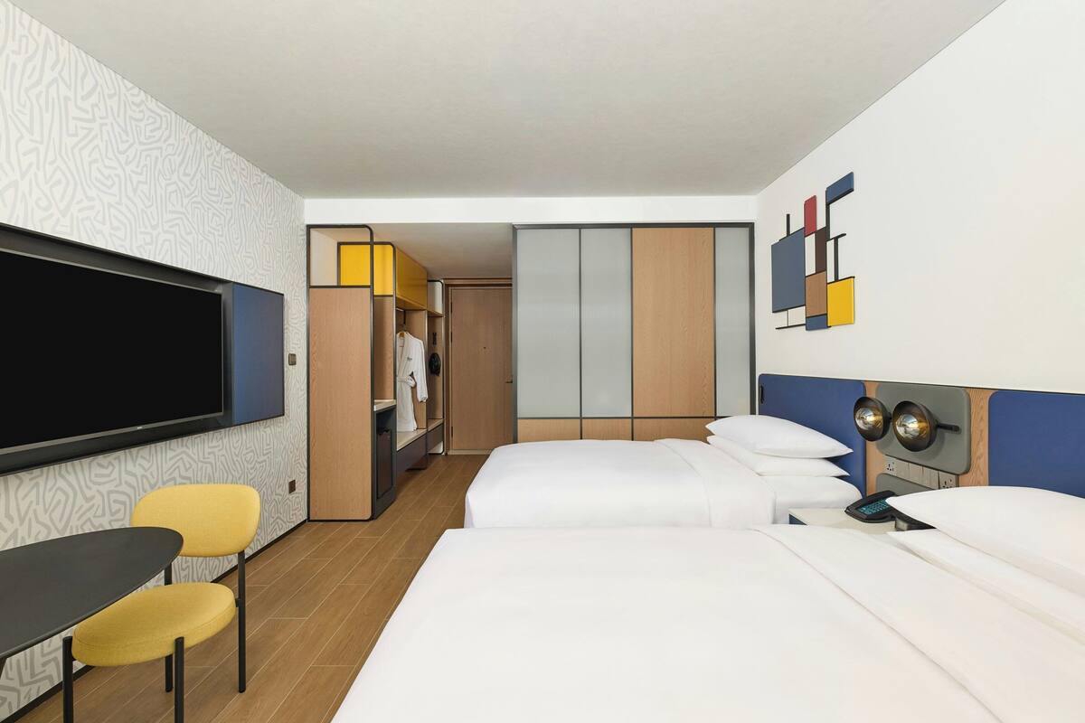 Quarto de hotel com televisão, duas camas, uma escrivaninha, uma cadeira e um guarda-roupa.