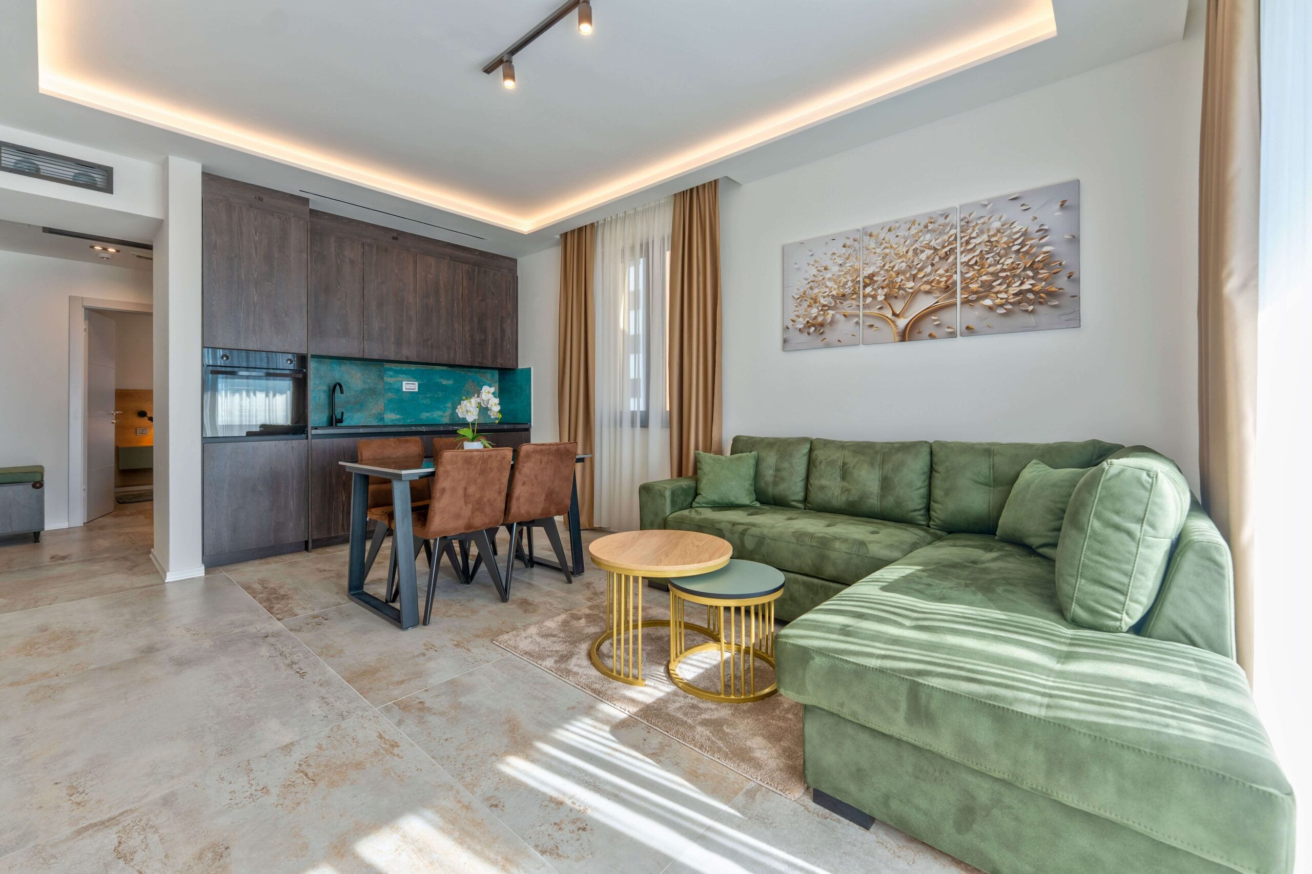 Uma sala moderna com um sofá verde, uma mesa de jantar com cadeiras e uma área de cozinha com armários de madeira e um painel de fundo verde-água.