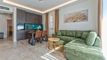 Uma sala moderna com um sofá verde, uma mesa de jantar com cadeiras e uma área de cozinha com armários de madeira e um painel de fundo verde-água.