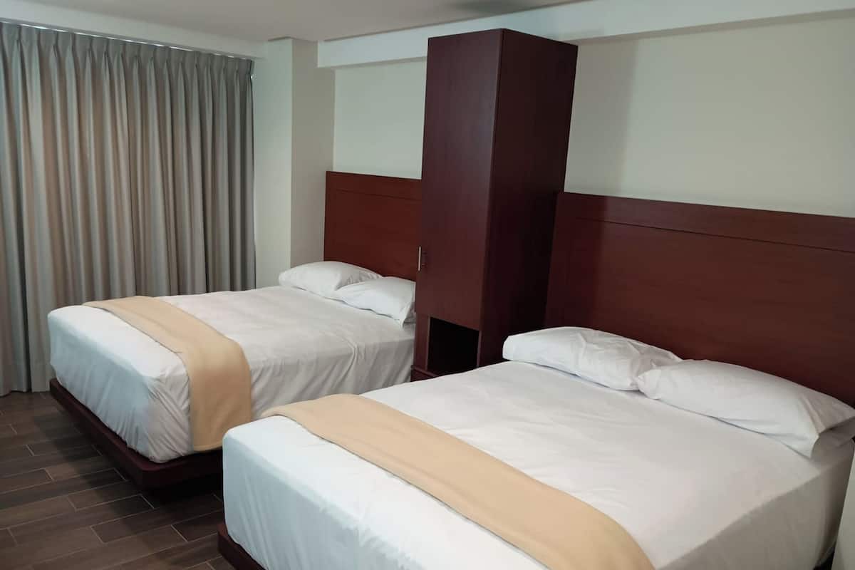 Duas camas de casal com cabeceiras de madeira, um guarda-roupa de madeira e uma janela com cortinas.