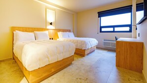 Quarto de hotel com duas camas, uma escrivaninha e uma janela grande.