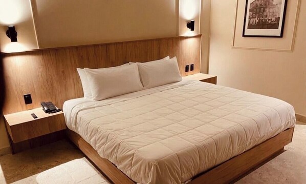 Cama bem arrumada com cabeceira de madeira, mesas de cabeceira com abajures e um quadro na parede.