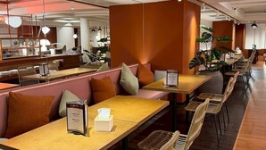 Um restaurante moderno com longas mesas de madeira, assentos acolchoados e diversos tipos de cadeiras.