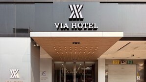 A entrada do VIA HOTEL, com um design moderno, incluindo um logotipo bem visível, uma porta de vidro e um pavimento ladrilhado.