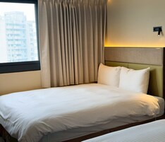 Quarto de hotel com uma cama grande, cabeceira, janela com cortinas e uma luminária fixada na parede.