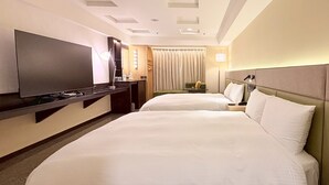 Quarto de hotel com duas camas, uma televisão de tela plana, uma escrivaninha com abajur e uma janela com cortinas.