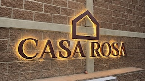 Pared de tijolos com uma placa que diz 'CASA ROSA' e uma pequena cascata.