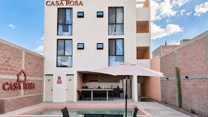 Edifício com a placa 'CASA ROSA', piscina, área de estar externa e cozinha aparente.