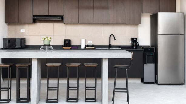 Cozinha moderna com armários de madeira escura, geladeira de aço inoxidável, micro-ondas embutido, cafeteira e área com banquetas.