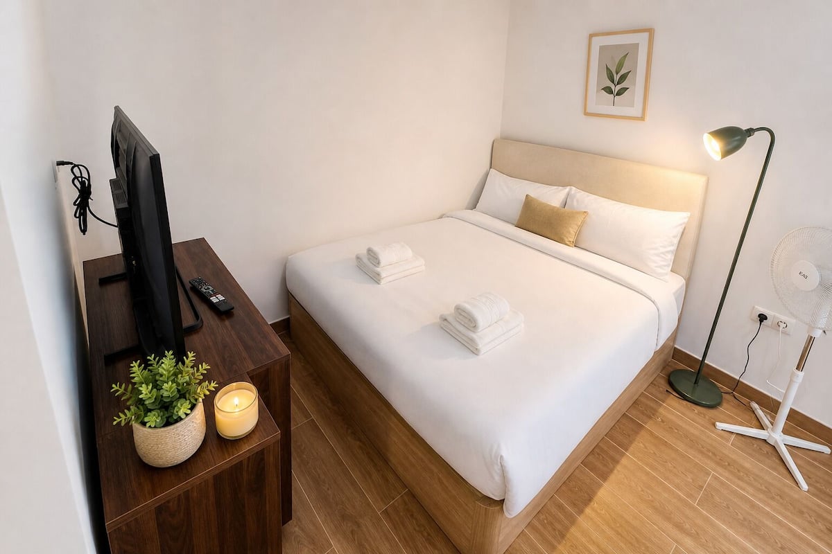 Quarto de hotel bem arrumado com cama, mesa de cabeceira, televisão e ventoinha.
