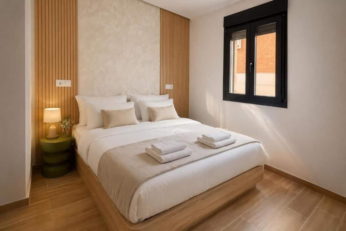 Quarto com cama, almofadas, mesa de cabeceira e uma janela.