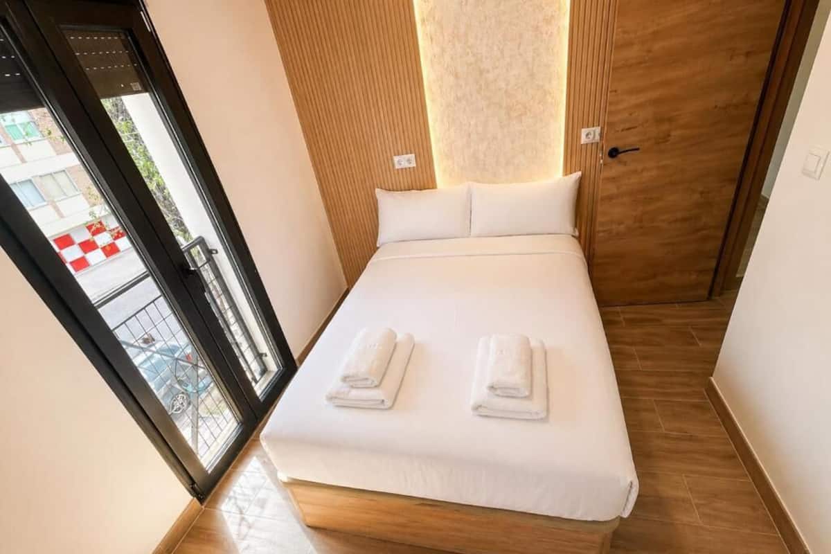 Quarto com uma cama, duas toalhas, uma porta de madeira e uma janela.